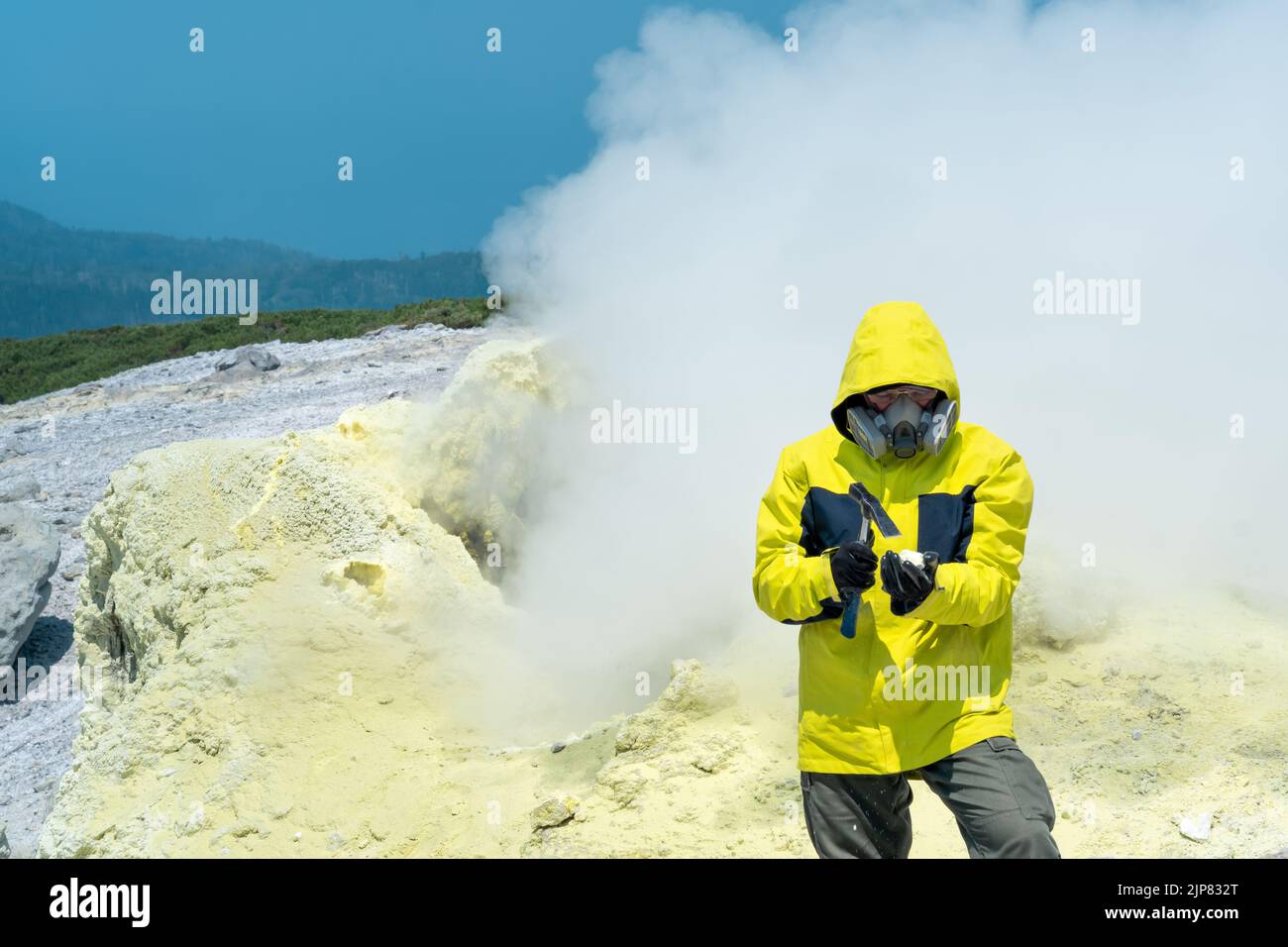 man volcano scientist on the background of a smoking fumarole examines ...