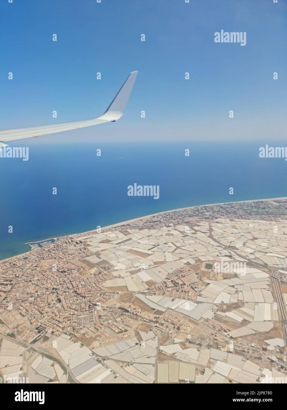 A vertical shot behind airplane window of the plane wing above seaside ...