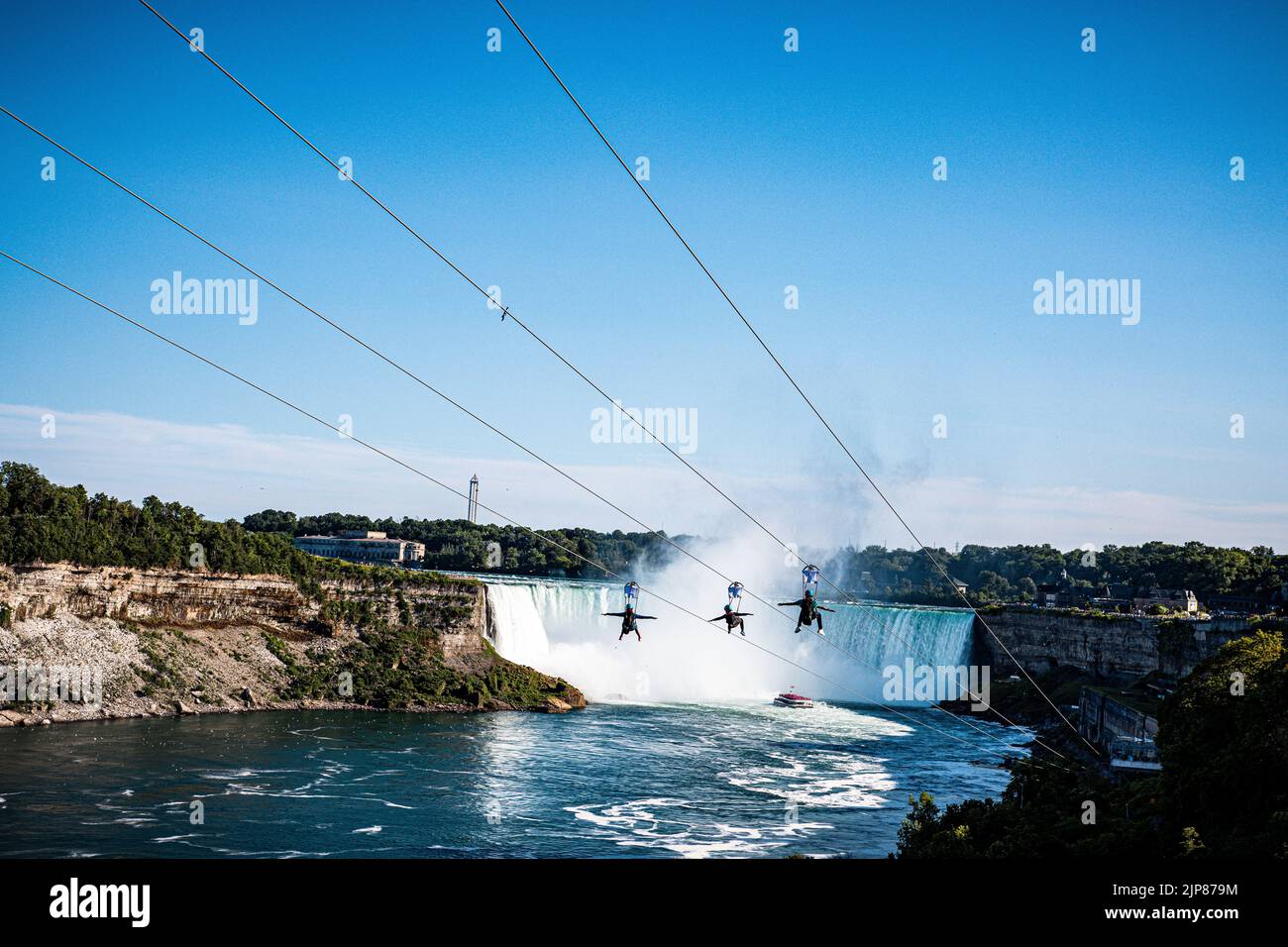 A back view of three people riding on the zipline above Niagara Falls ...