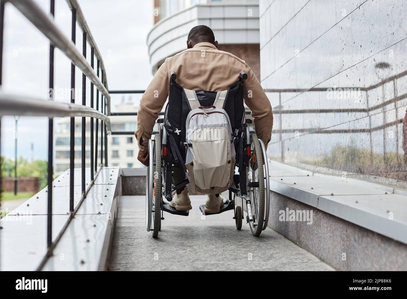 Back view of man with disability pushing wheelchair wheel while going ...