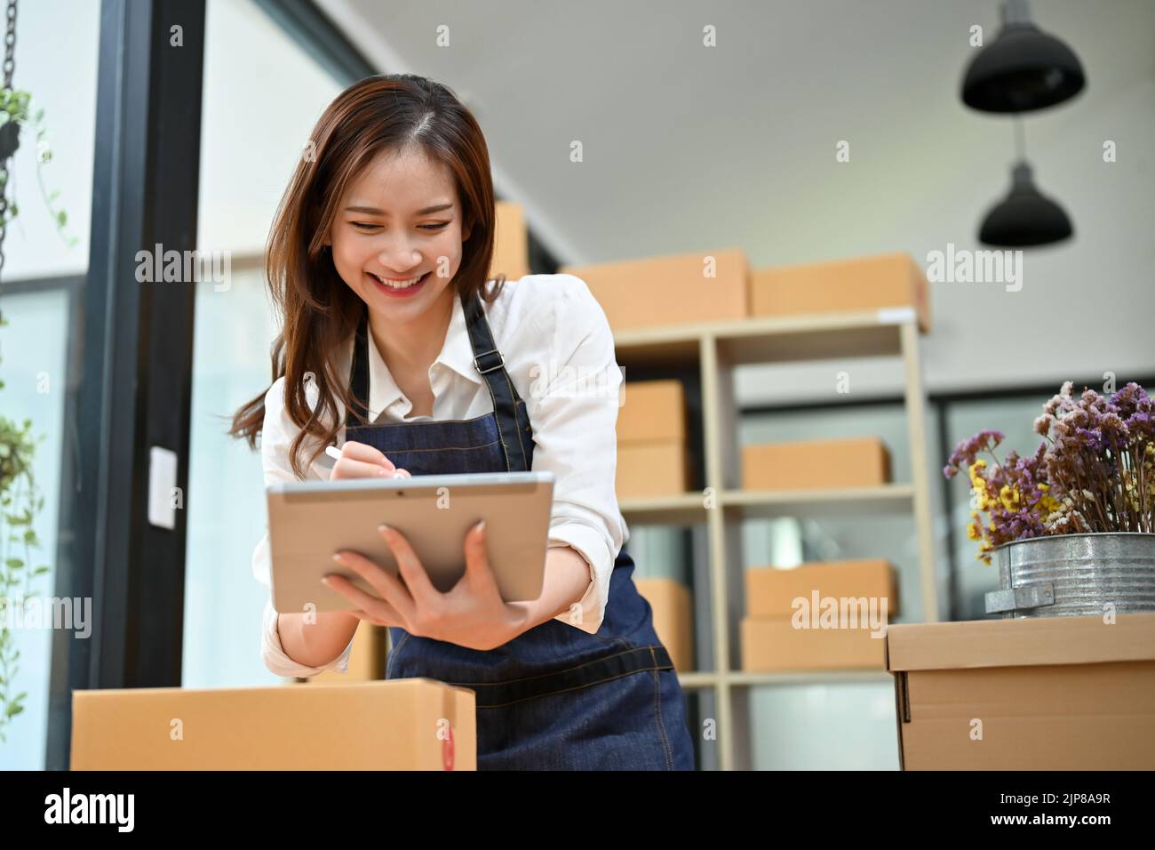 Attractive young Asian female e-commerce business owner using tablet ...