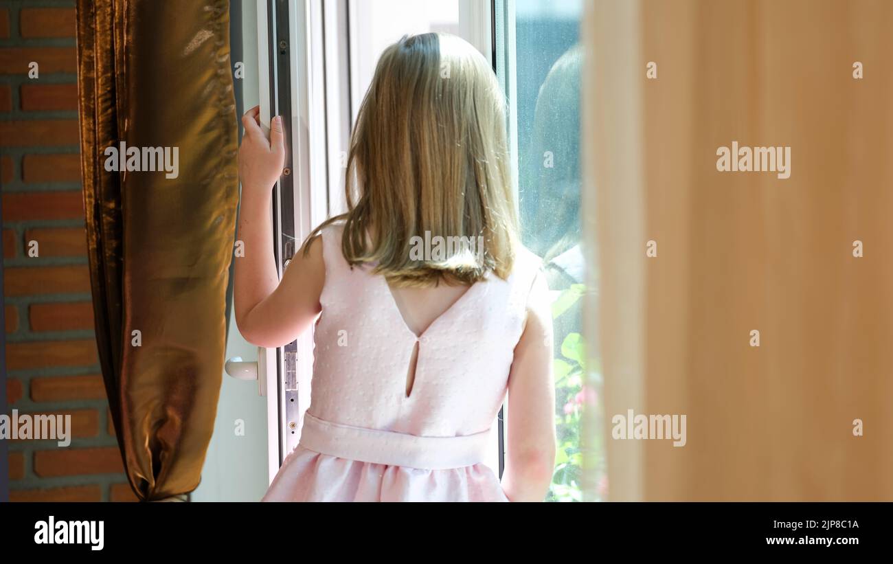 Girl in pink dress standing on windowsill at open window Stock Photo ...