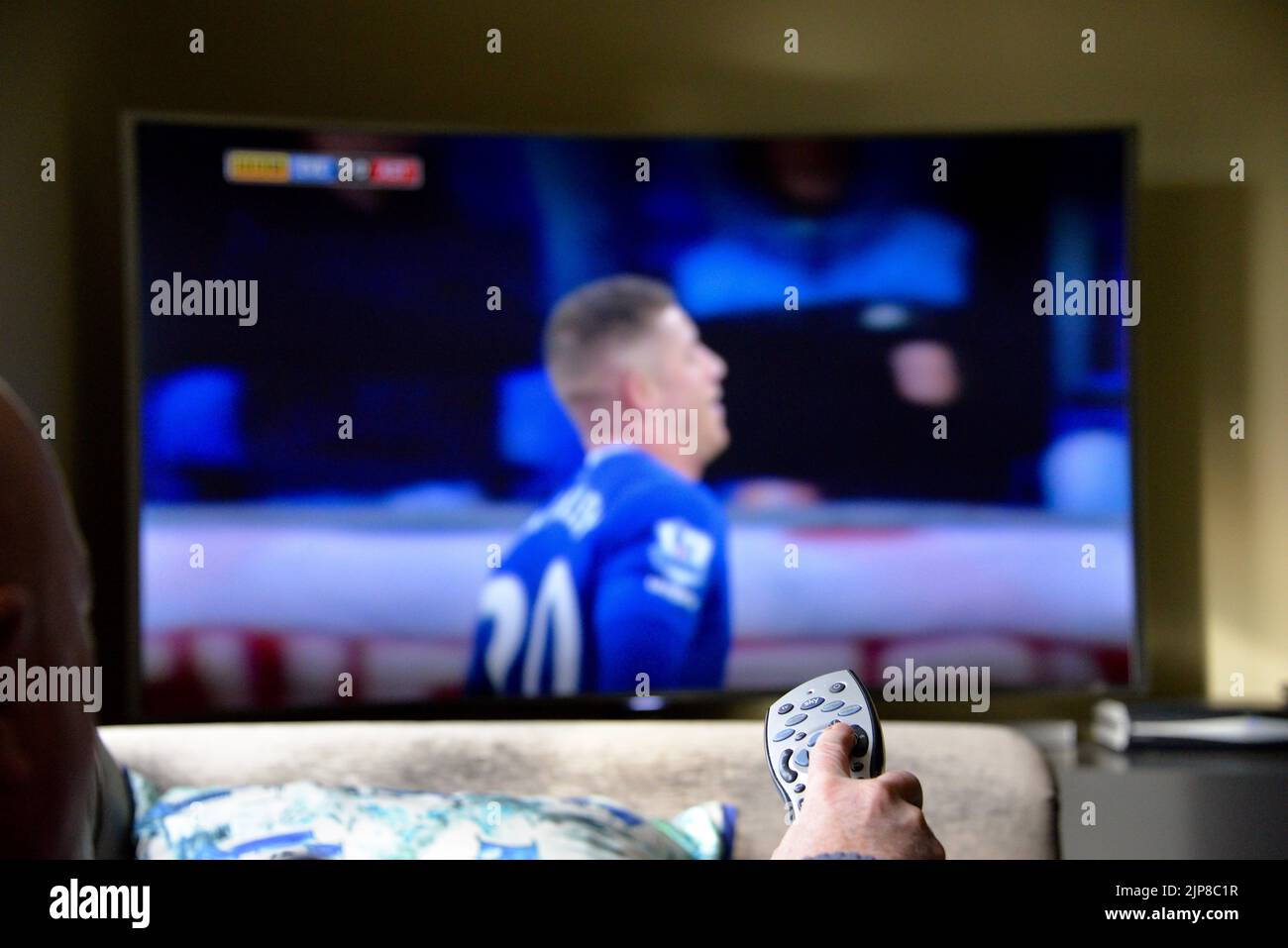 A hand presing a button on the remote control in front of a television ...