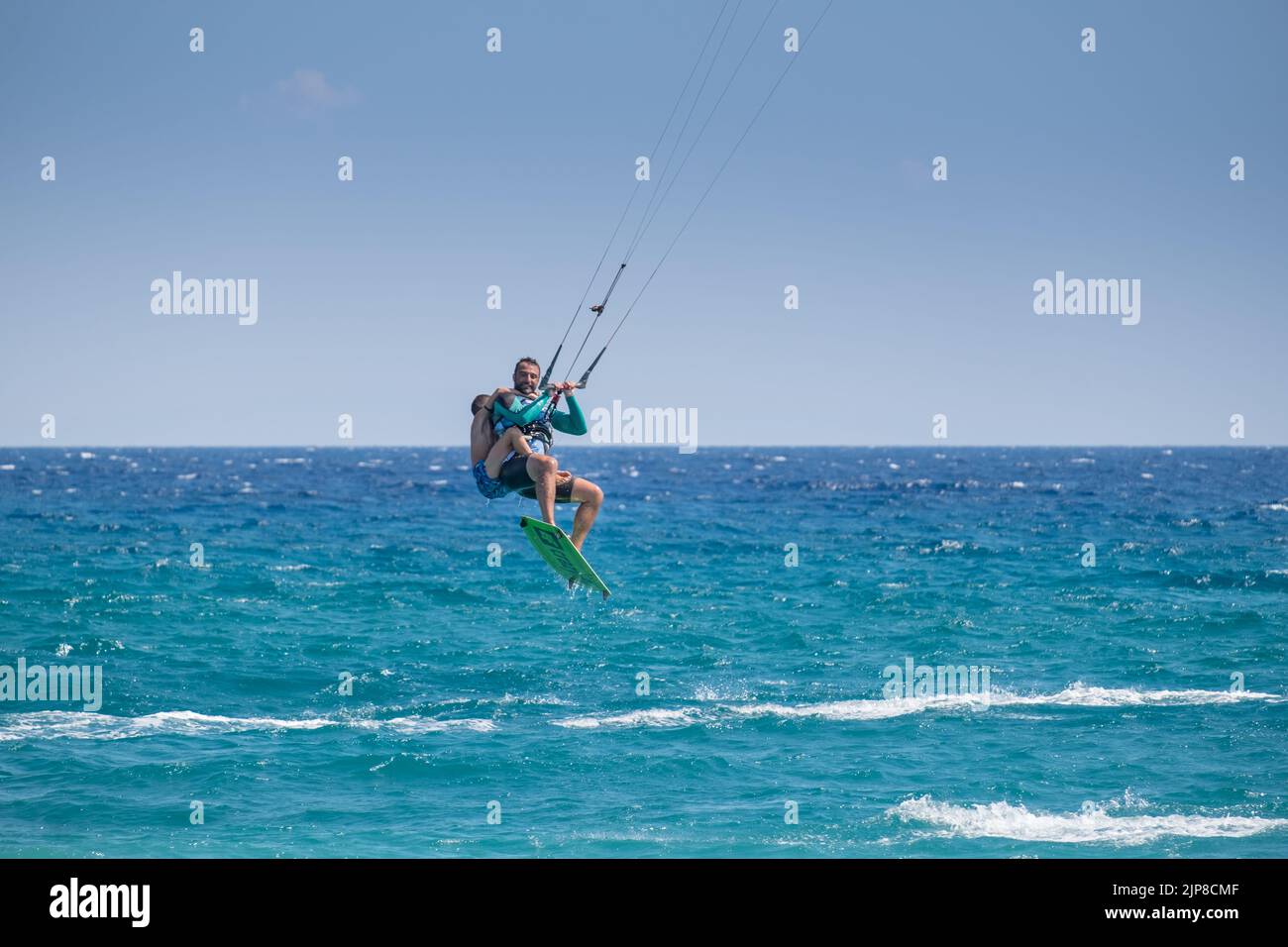Man kitesurfing and jumping in the air with a young boy in his back at ...