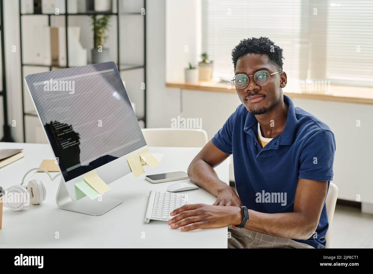 Portrait of African young developer in eyeglasses looking at camera ...