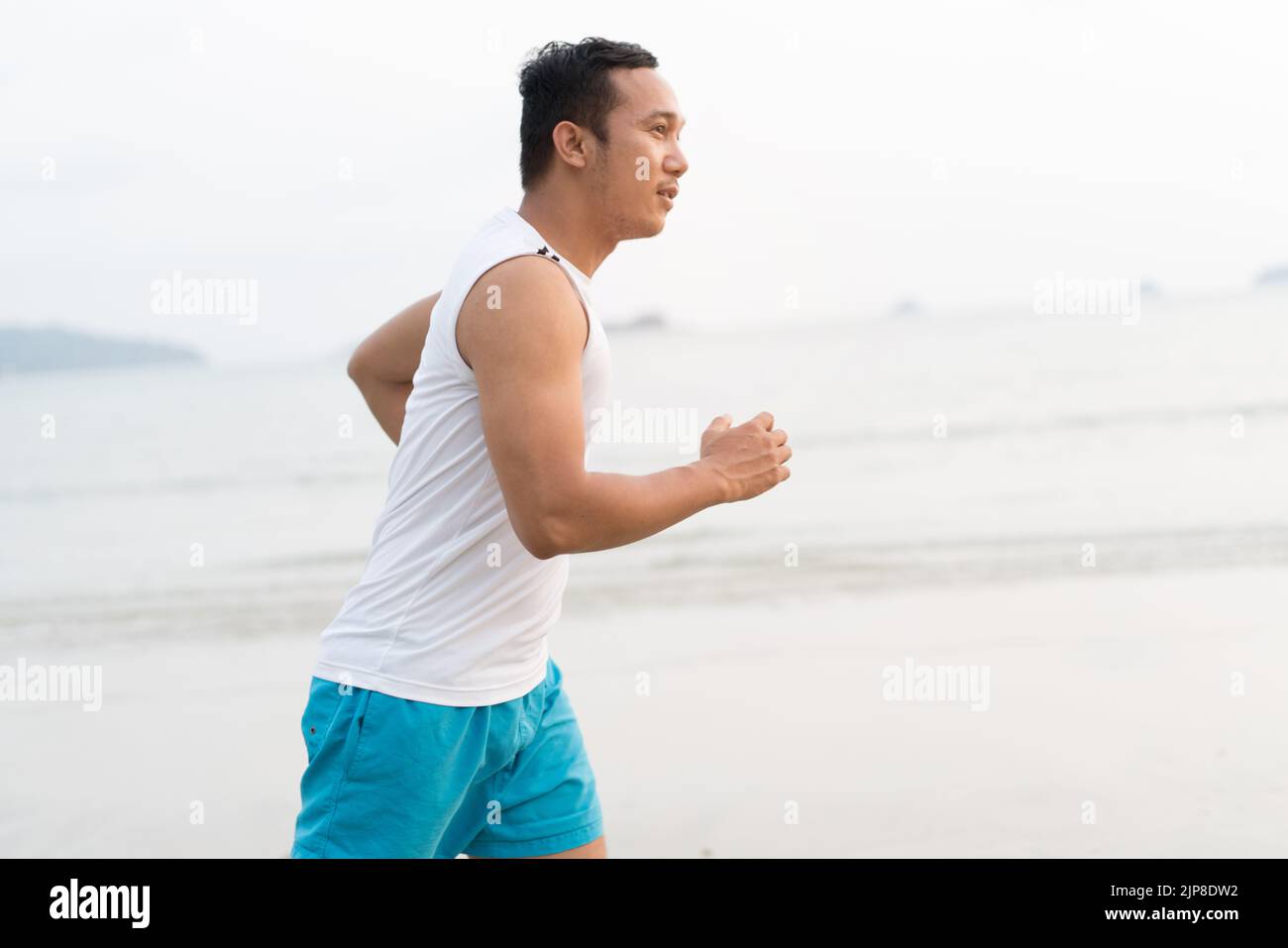 asian sport man running along seaside. running on beach with healthy ...