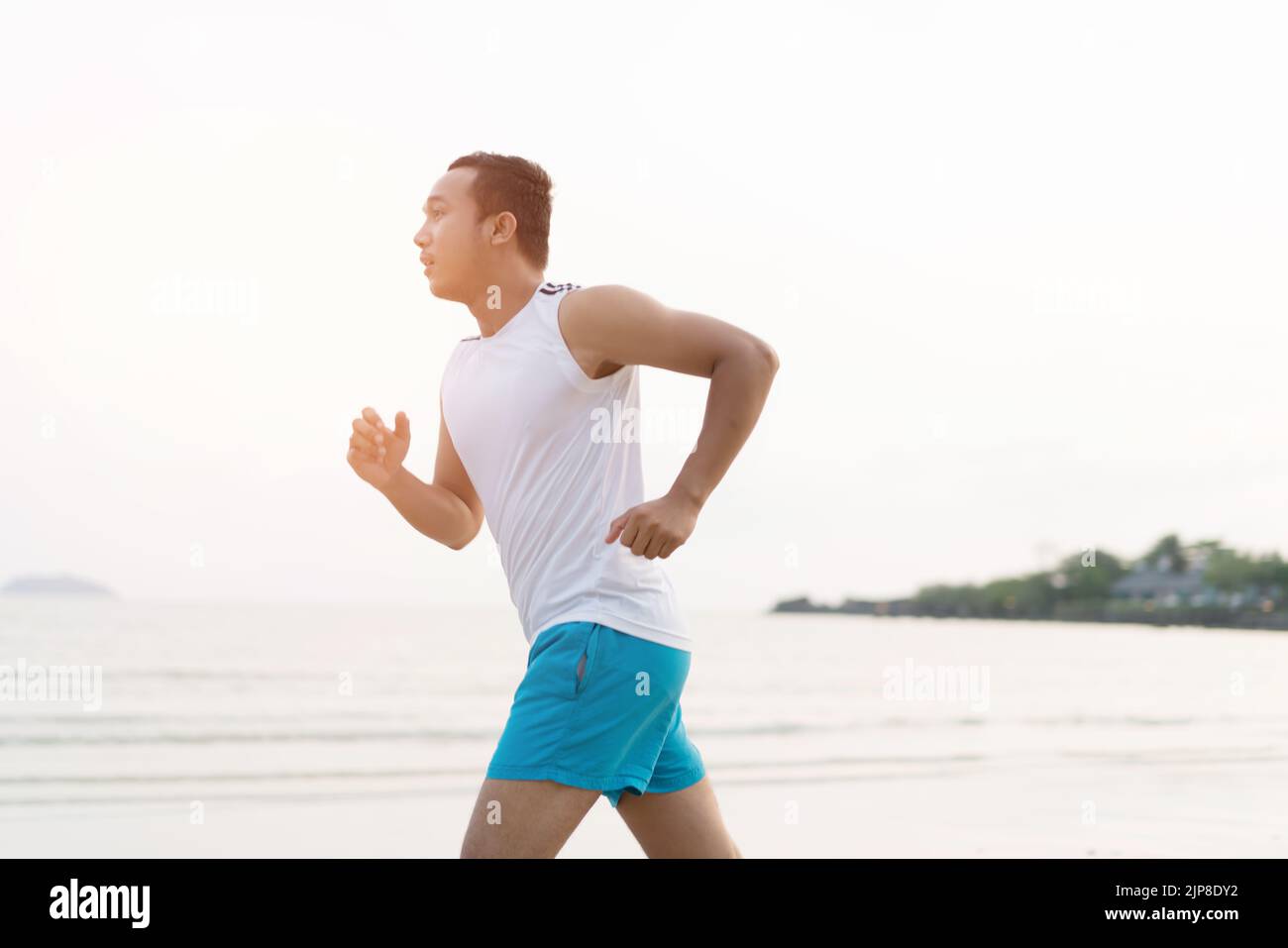 asian sport man running along seaside. running on beach with healthy ...