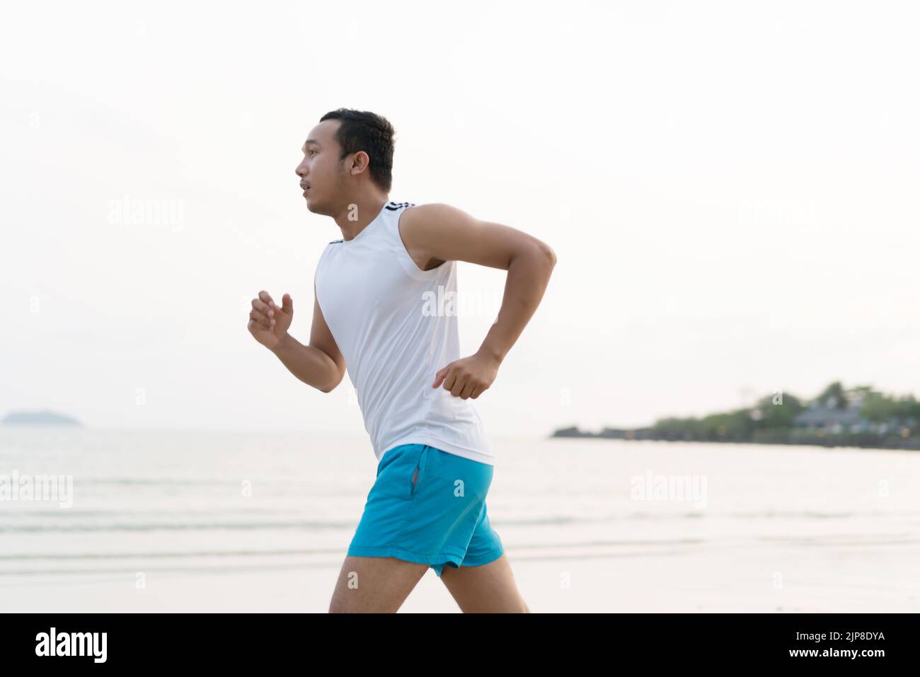 asian sport man running along seaside. running on beach with healthy ...