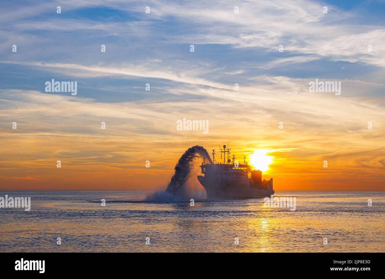 Vessel engaged in dredging at sunset time. Hopper dredger working at ...