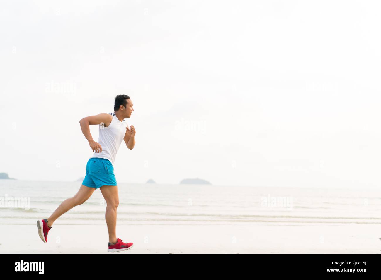 asian sport man running along seaside. running on beach with healthy ...