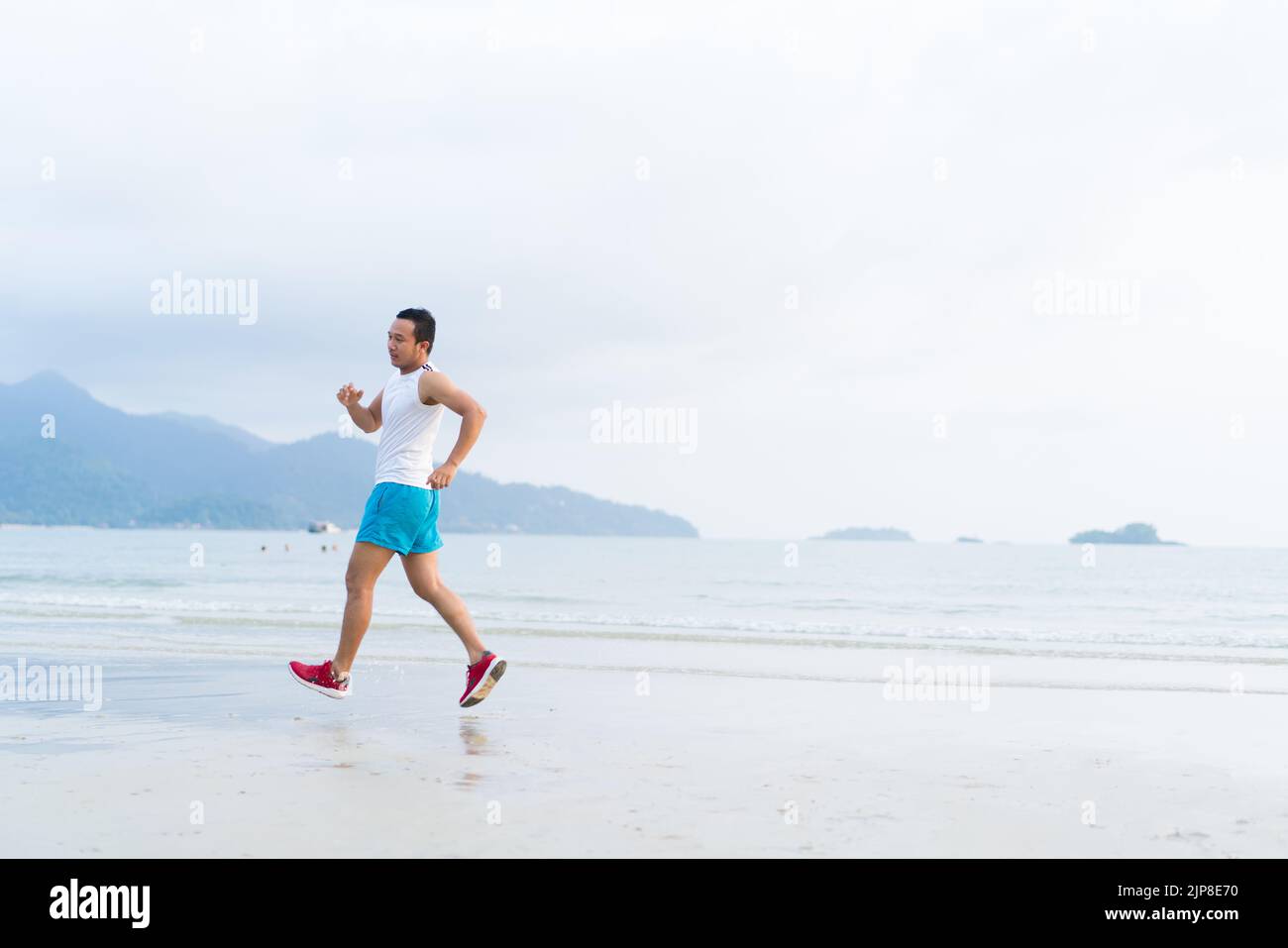 asian sport man running along seaside. running on beach with healthy ...