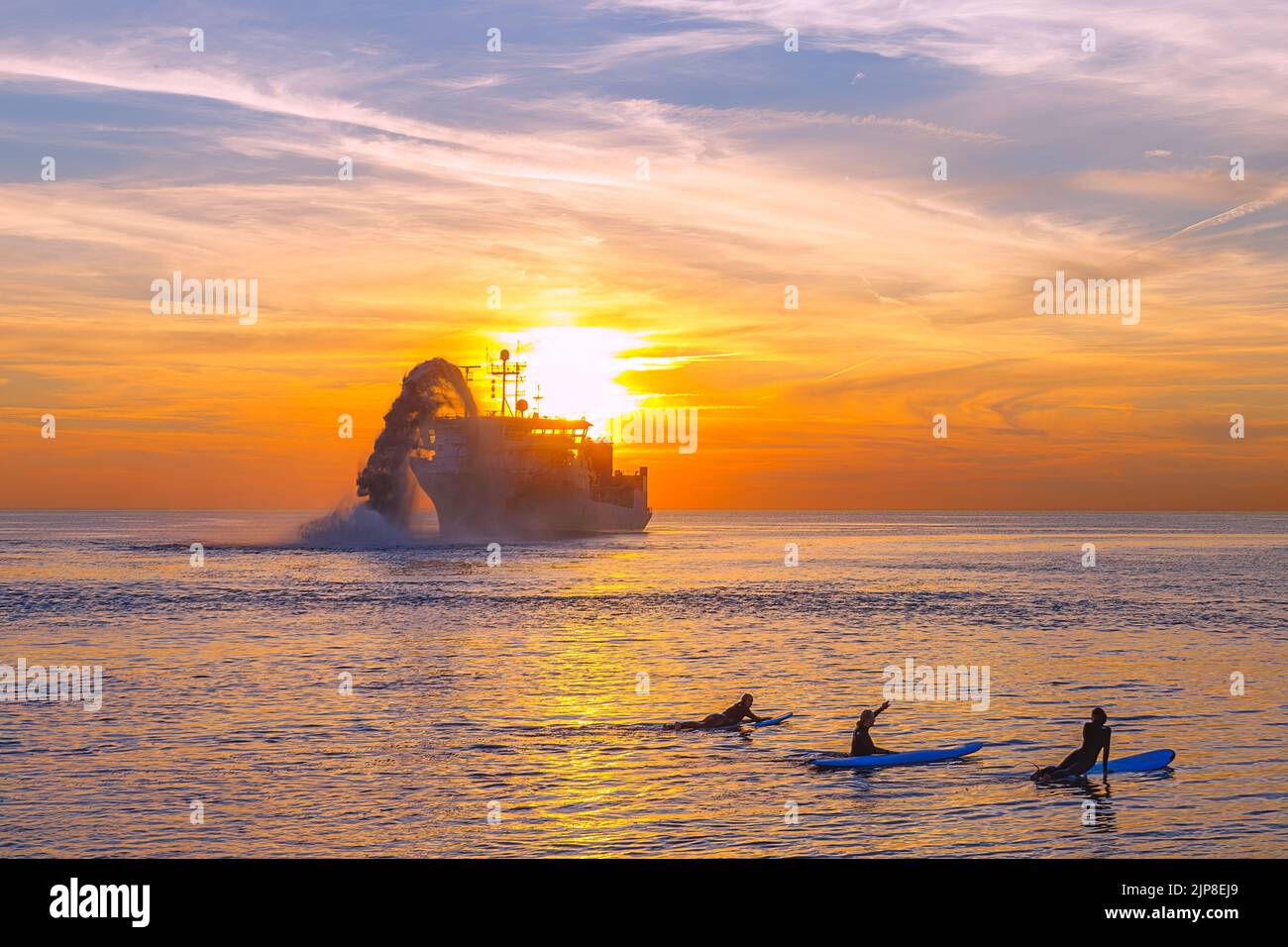Vessel engaged in dredging at sunset time. Hopper dredger working at ...