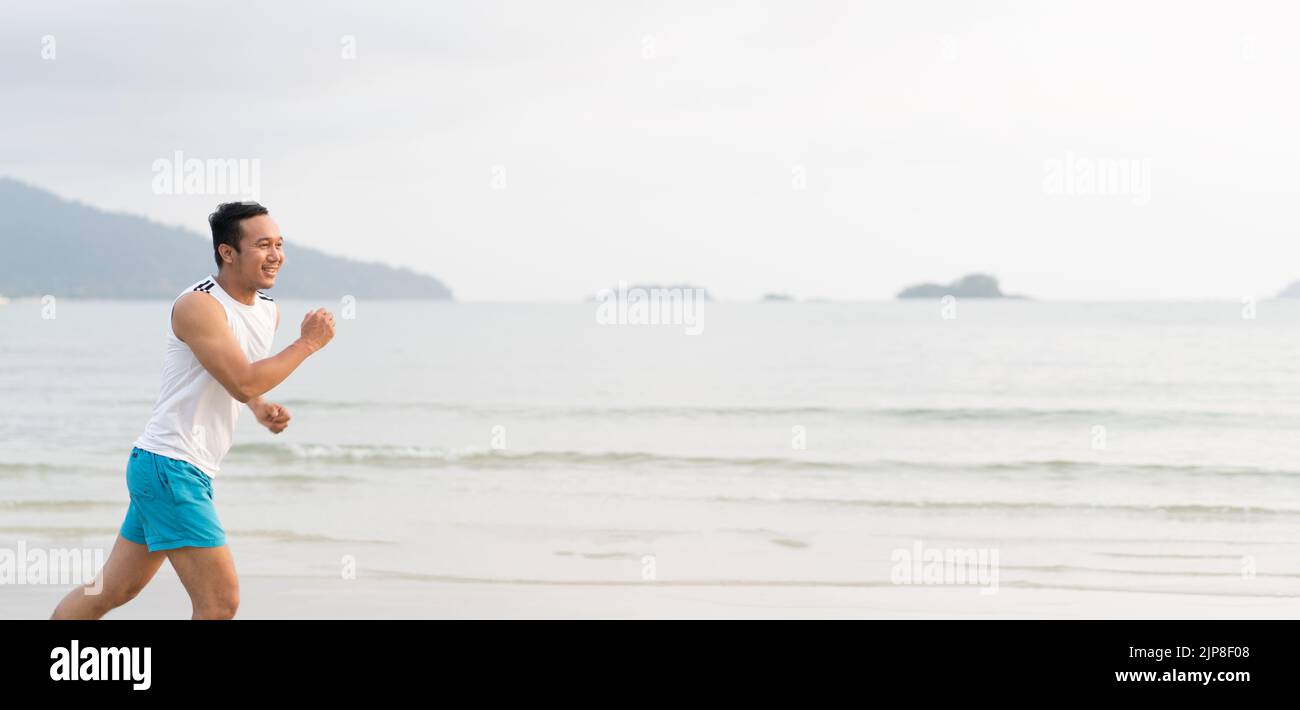 asian sport man running along seaside. running on beach with healthy ...