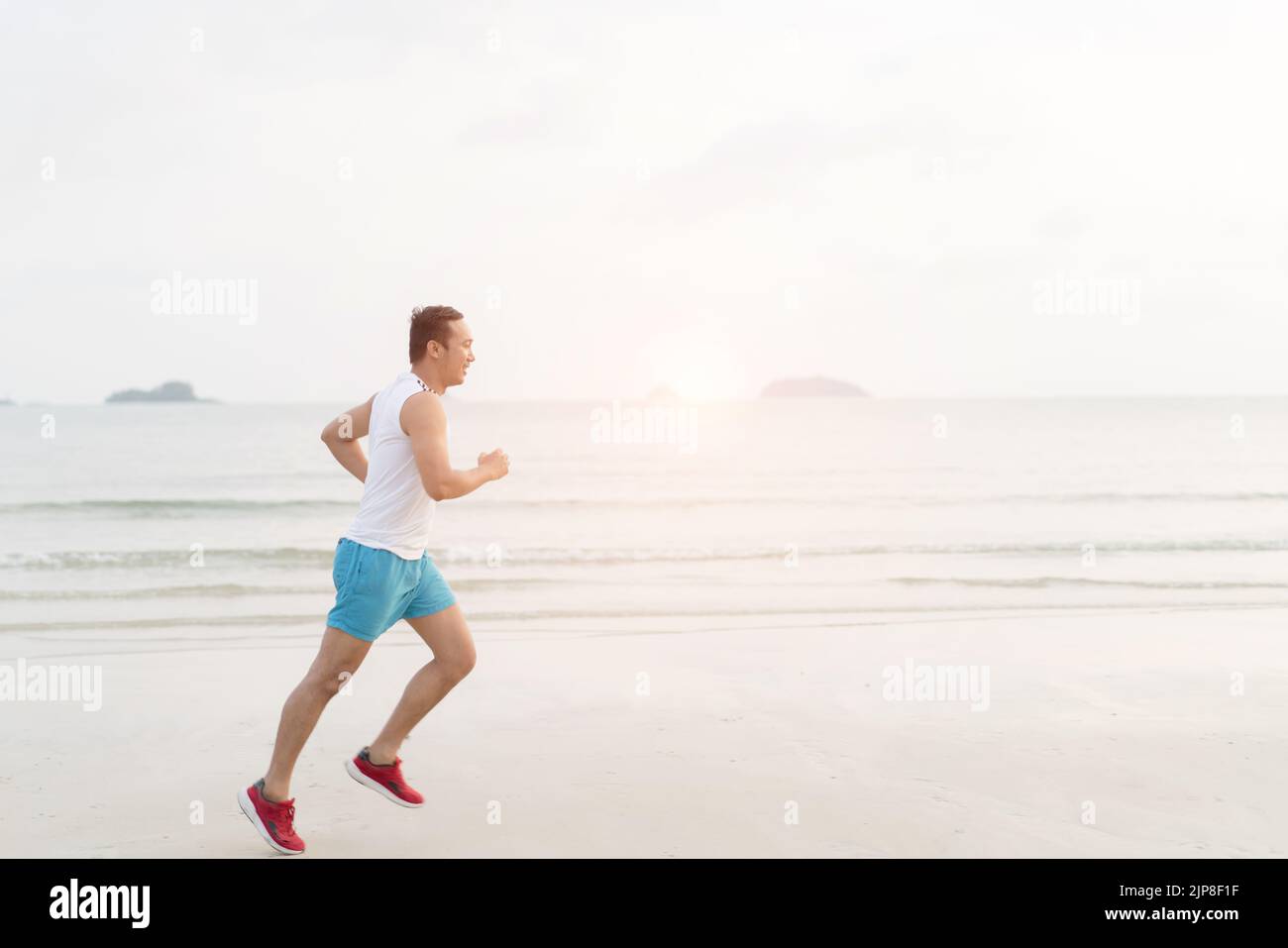 asian sport man running along seaside. running on beach with healthy ...