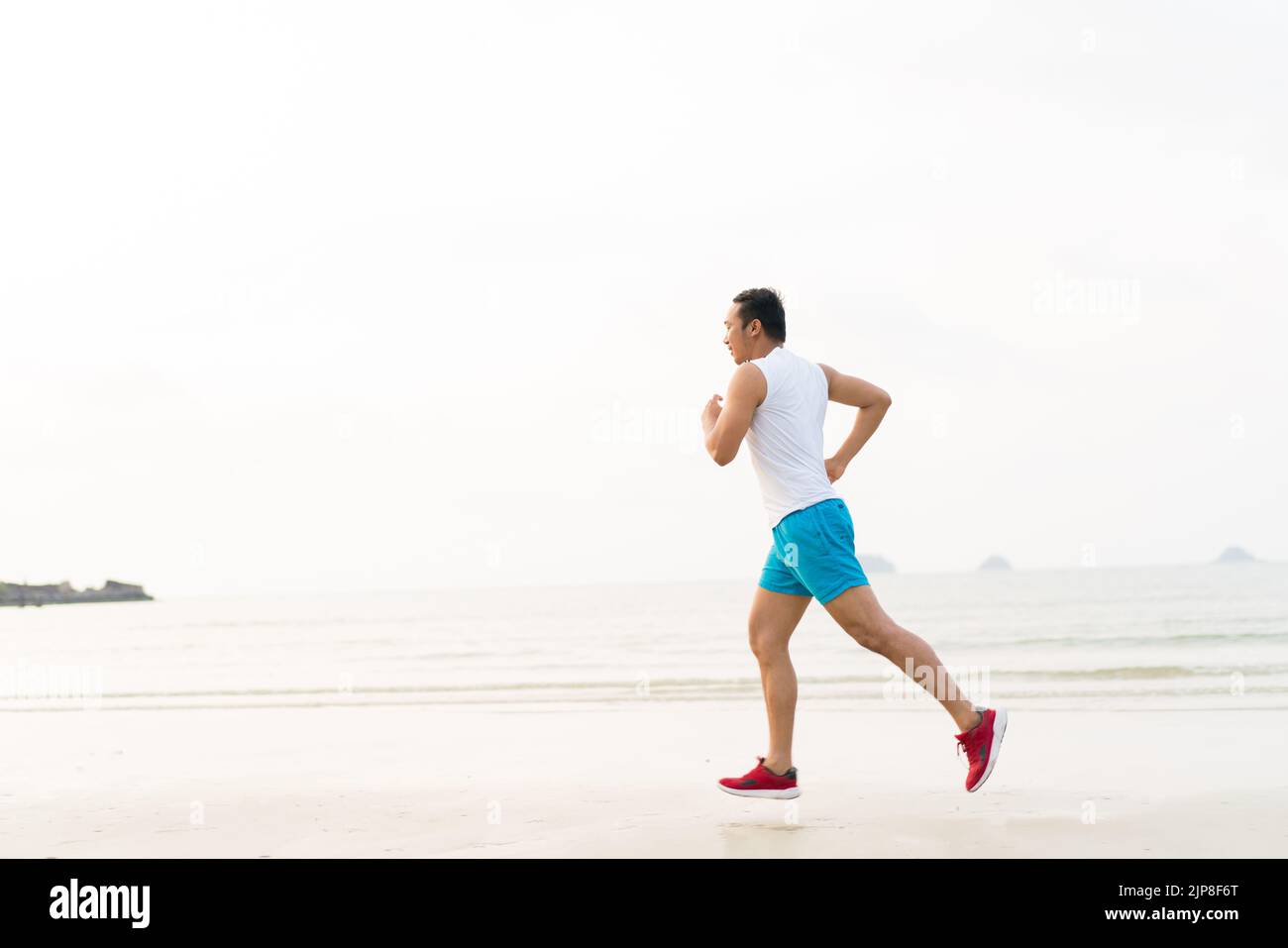 asian sport man running along seaside. running on beach with healthy ...