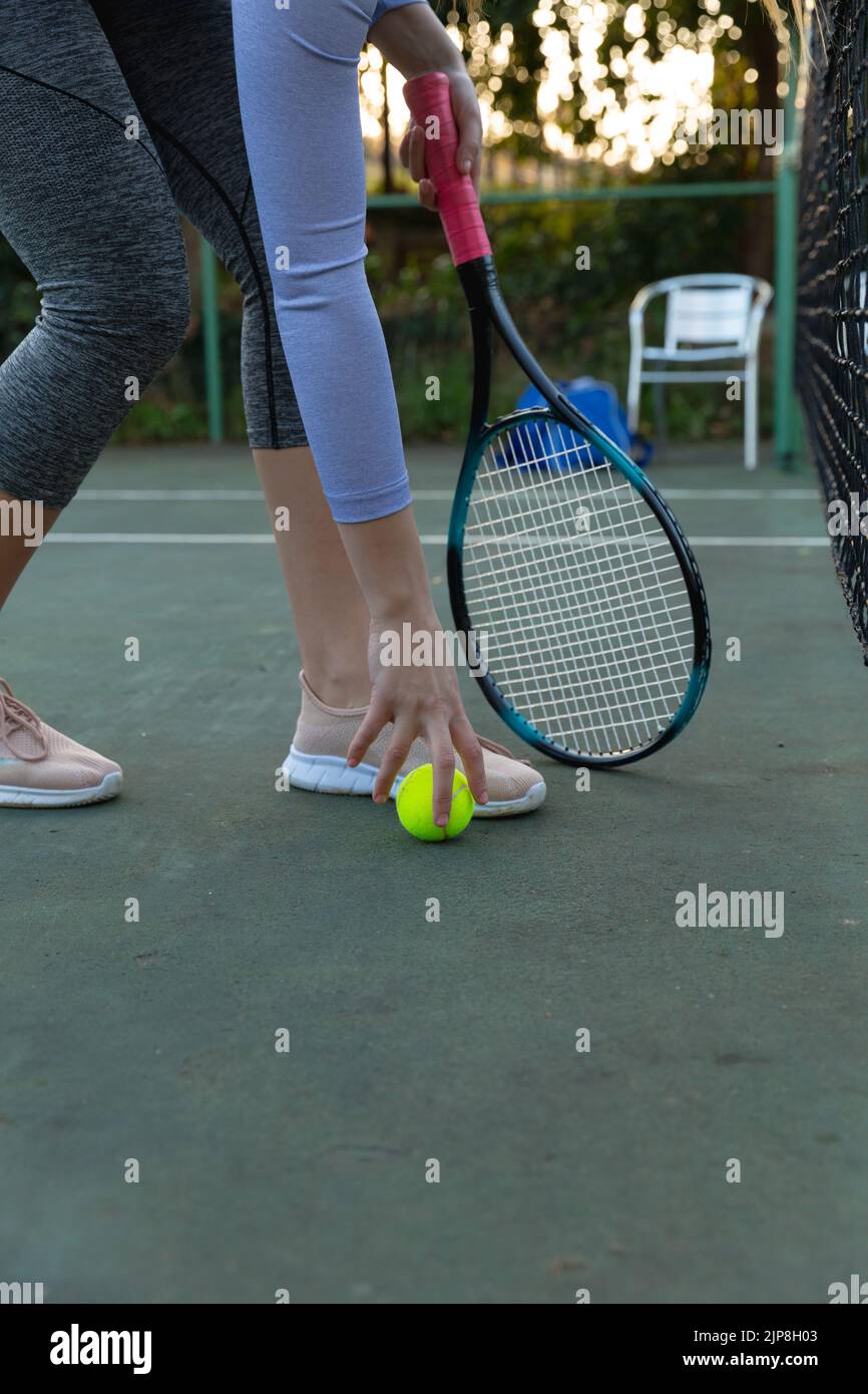 Low section of woman holding tennis racket picking up ball on outdoor ...