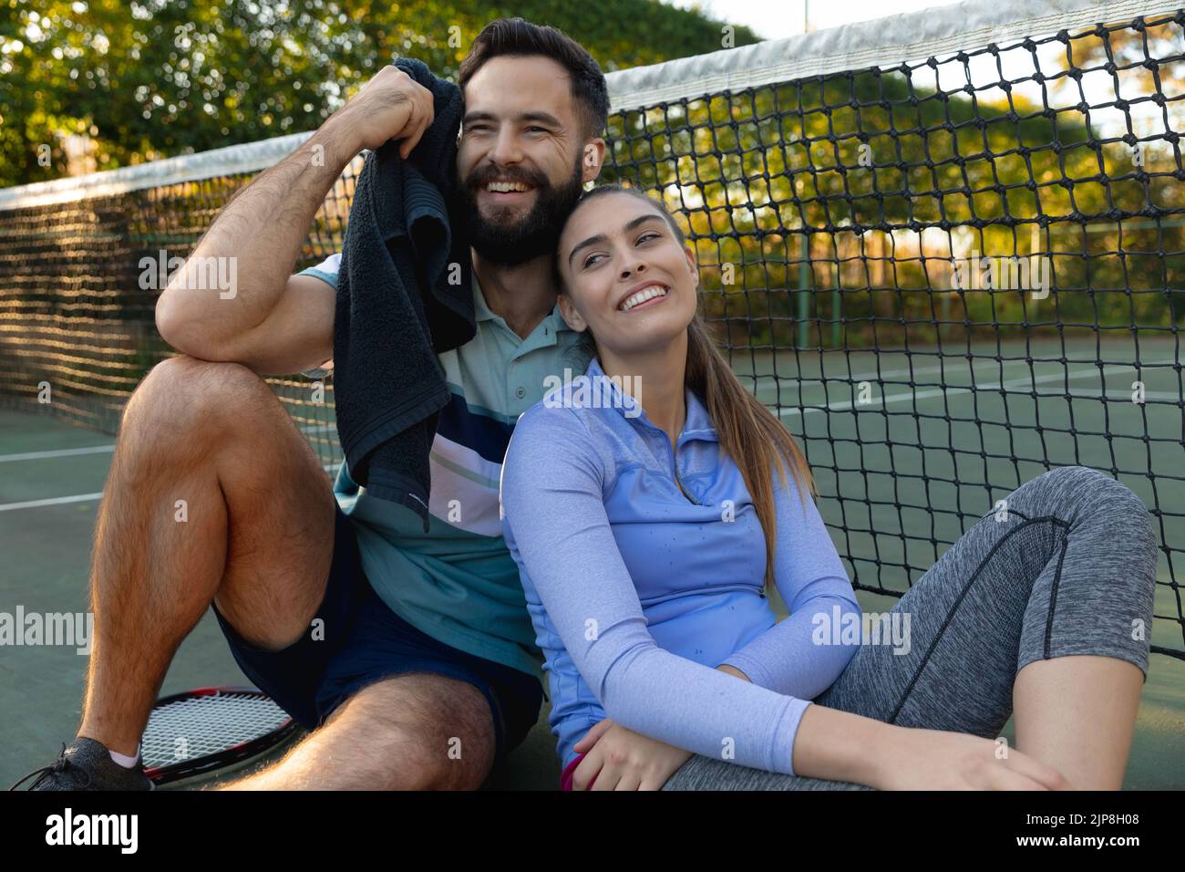 Happy caucasian couple sitting on outdoor tennis court by net ...