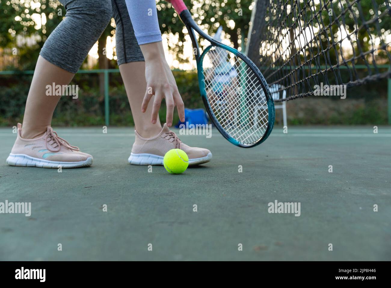 Low section of woman holding tennis racket picking up ball on outdoor ...