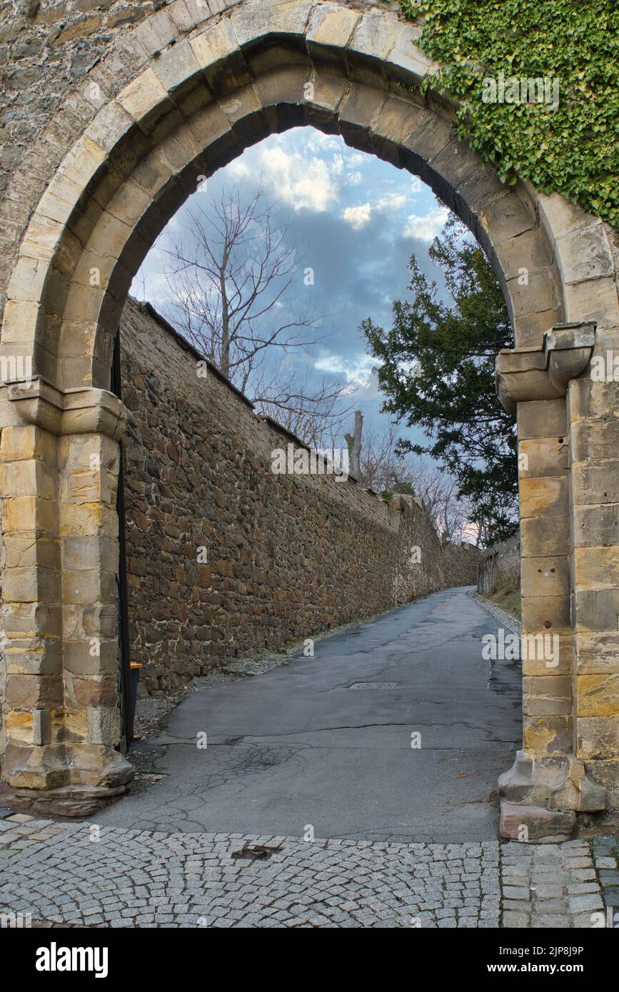 A vertical closeup of a long asphalt path under a stone arch on the ...