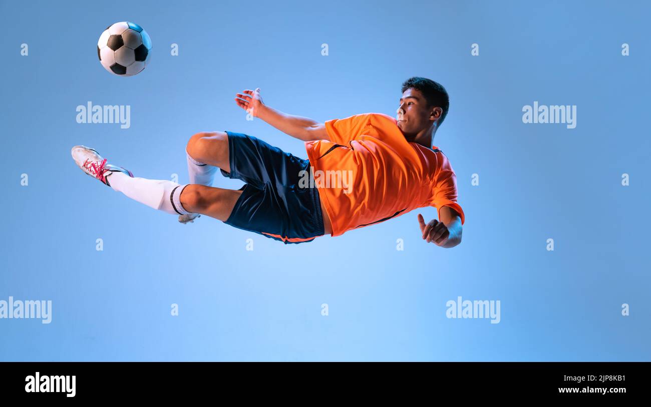 Dynamic portrait of young male football player training, kicking ball ...