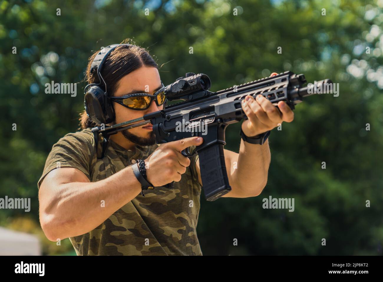White muscular man in camouflage t-shirt and safety gear firing ...
