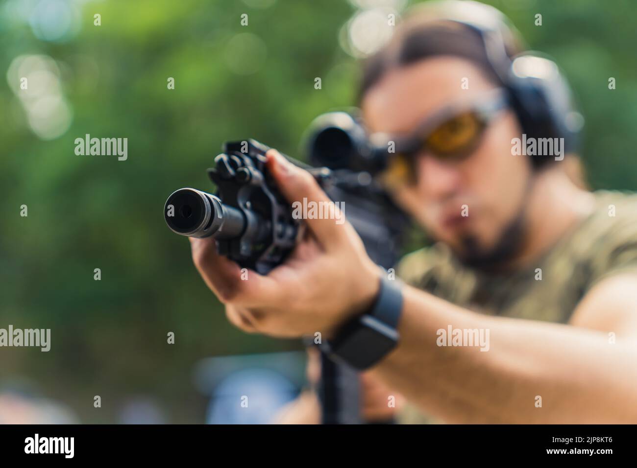 Man wearing camouflage t-shirt safety headphones and goggles aiming ...