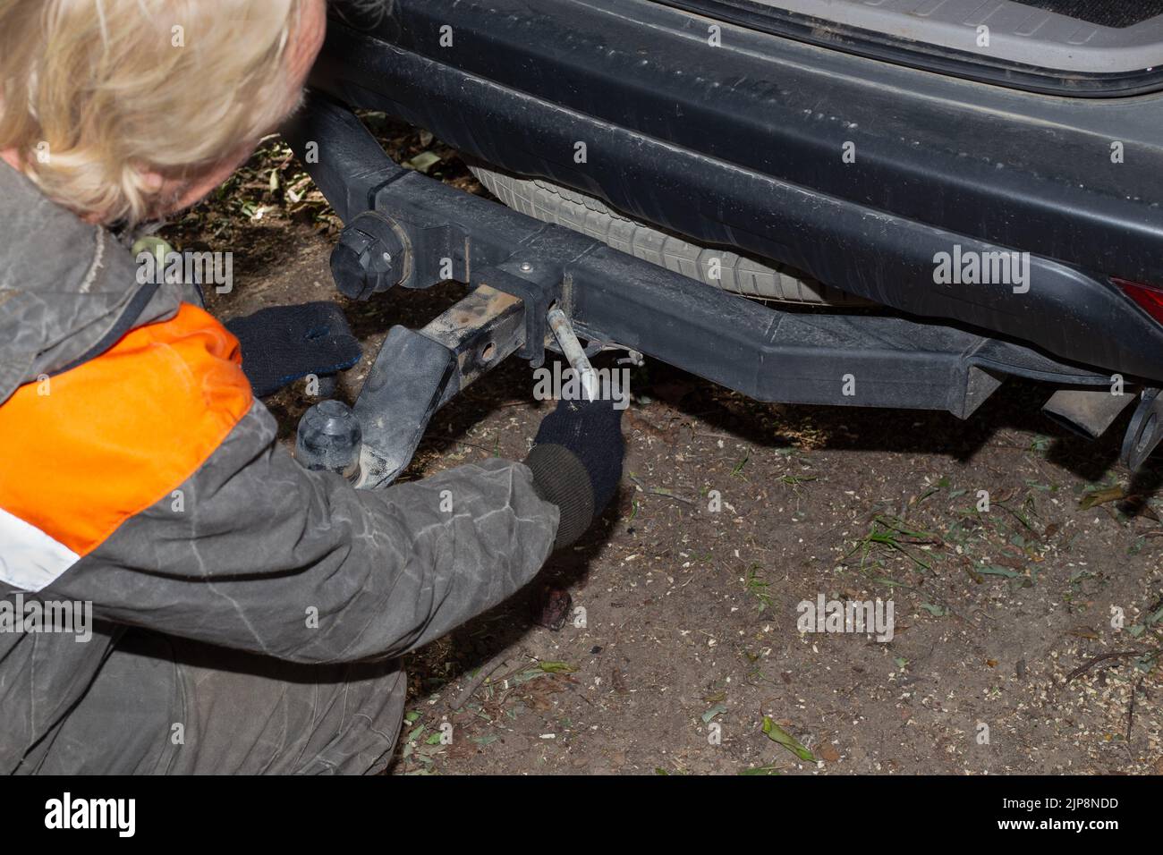 A man mounts the hook of an iron towbar on a car for towing a trailer ...