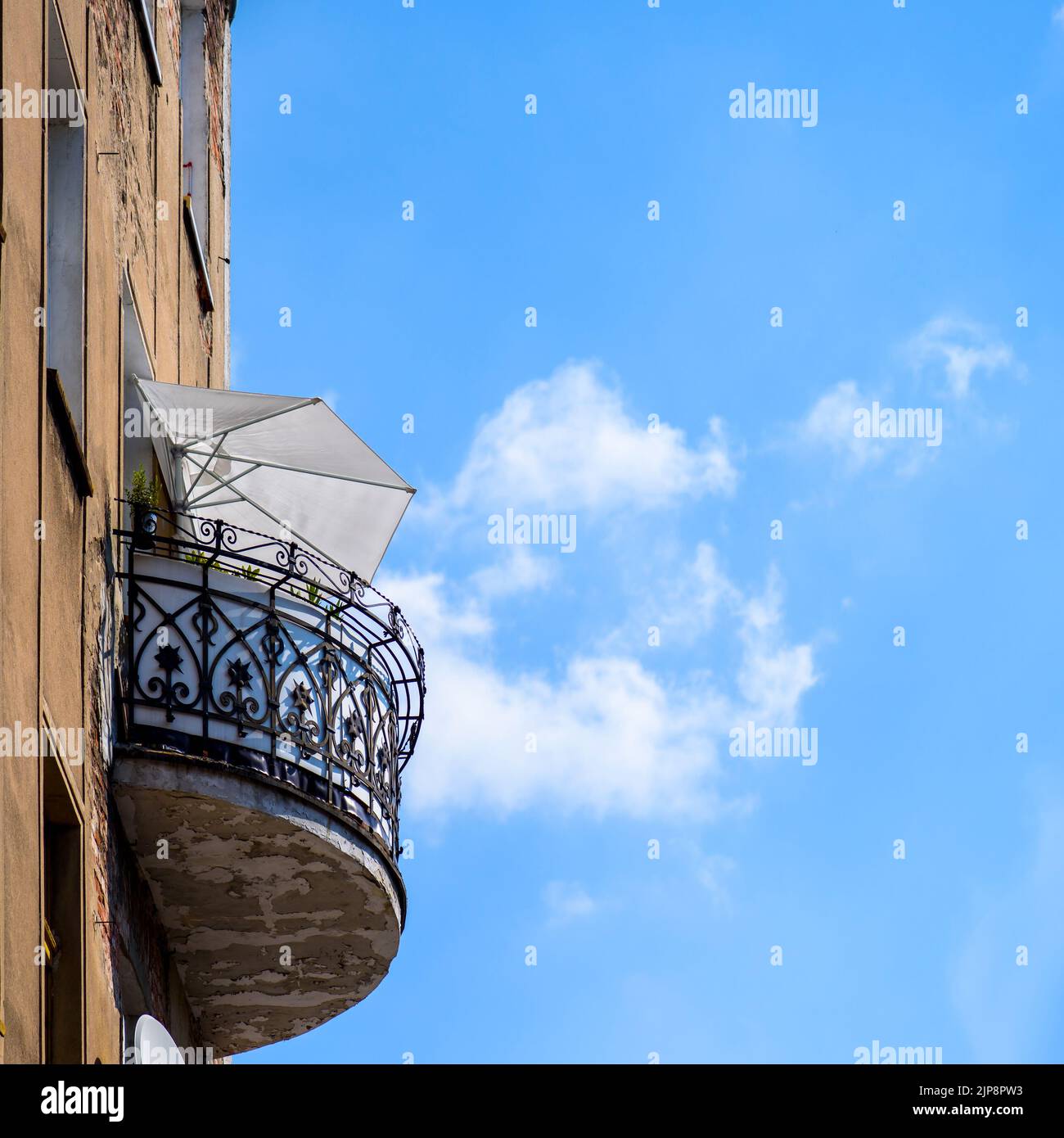 Old balcony with open umbrella on a facade of building on a blue sky ...