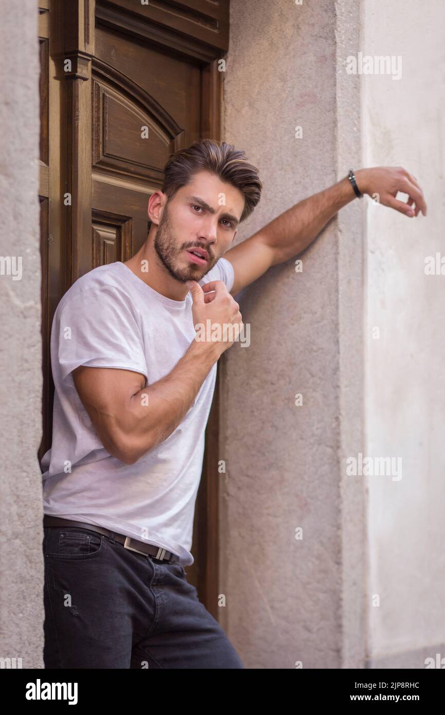 Metrosexual male in white t shirt and jeans standing with hand at chin ...