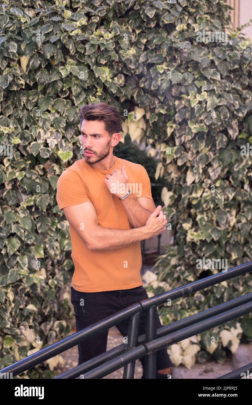 Metrosexual male with fit body in orange t shirt and jeans standing on ...
