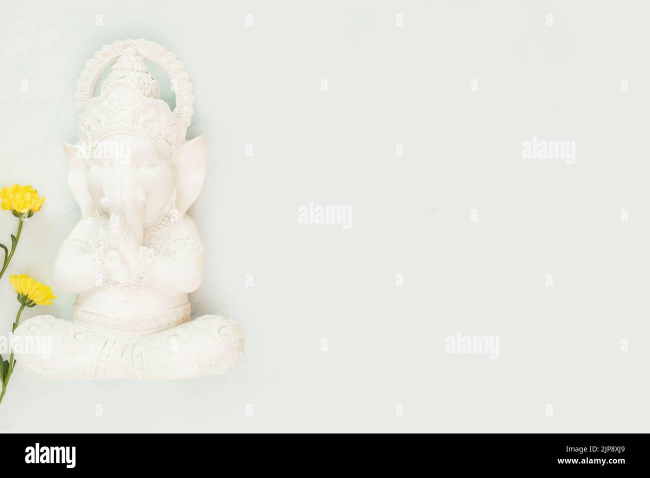 Sculpture of Lord Ganesha with flowers on a light blue background with ...