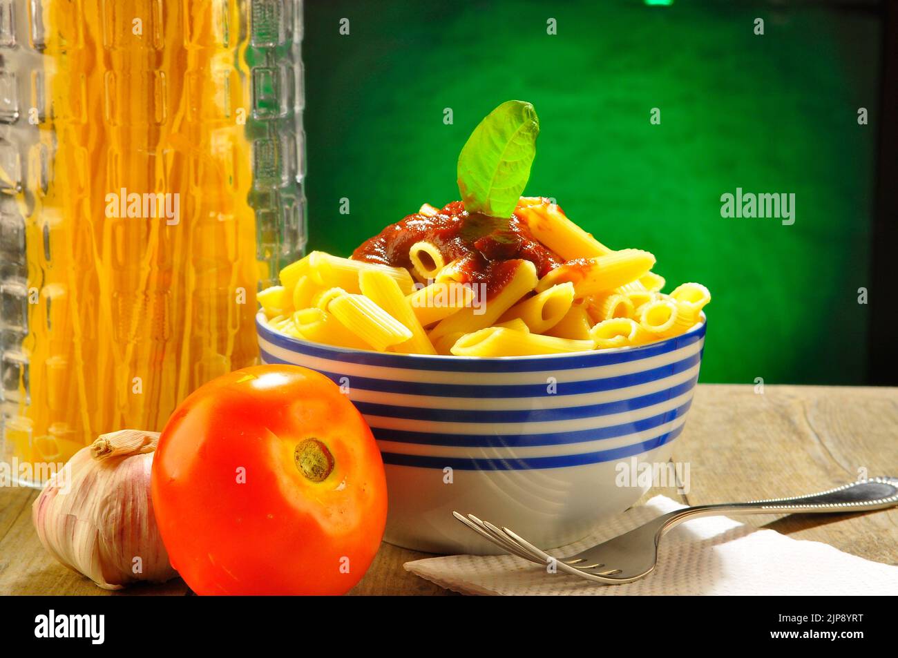 Still life with penne pasta meal with tomato and fork on green ...