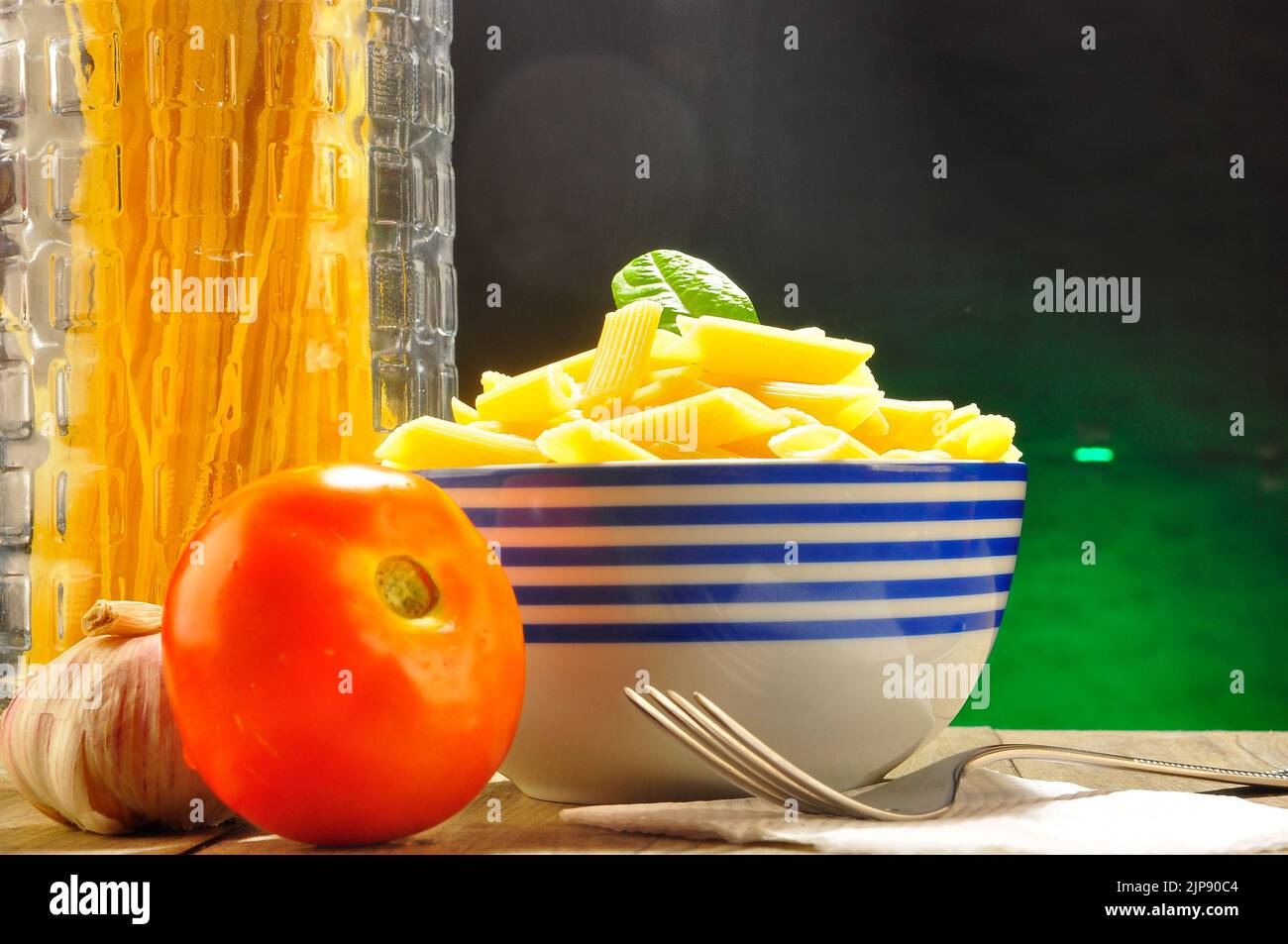 Still life with penne pasta meal with tomato and fork on green ...