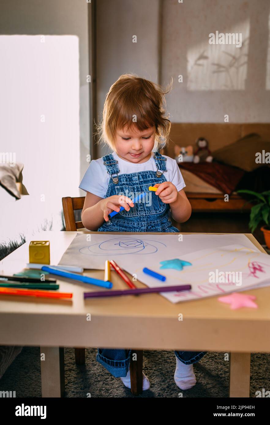 Small child at home at the children's table draws with felt-tip pens ...