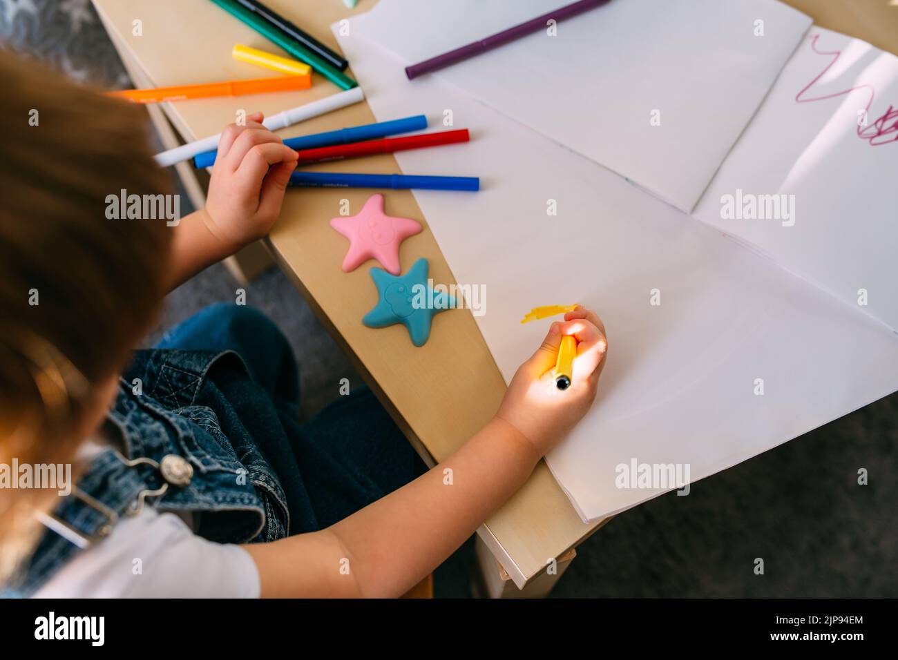 Small child at home at the children's table draws with felt-tip pens ...