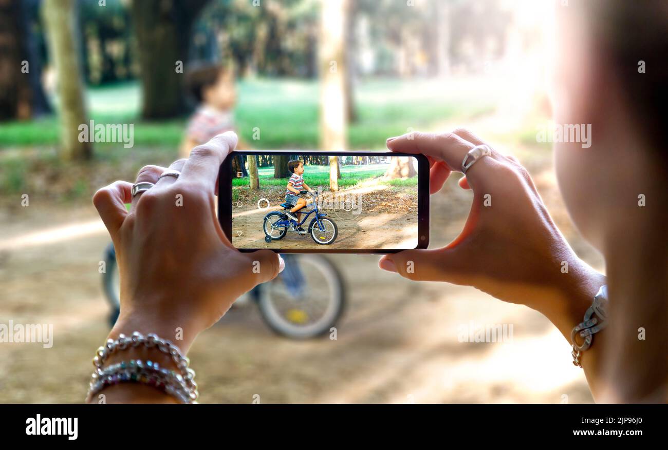 Woman photographing her little son with a cell phone. The child is ...