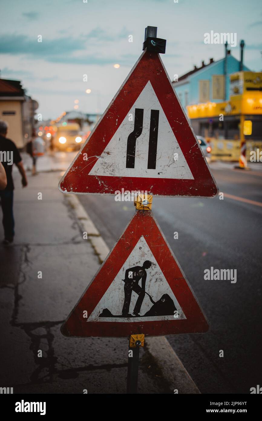 A vertical shot of red triangular safety signs of a narrowing road and ...