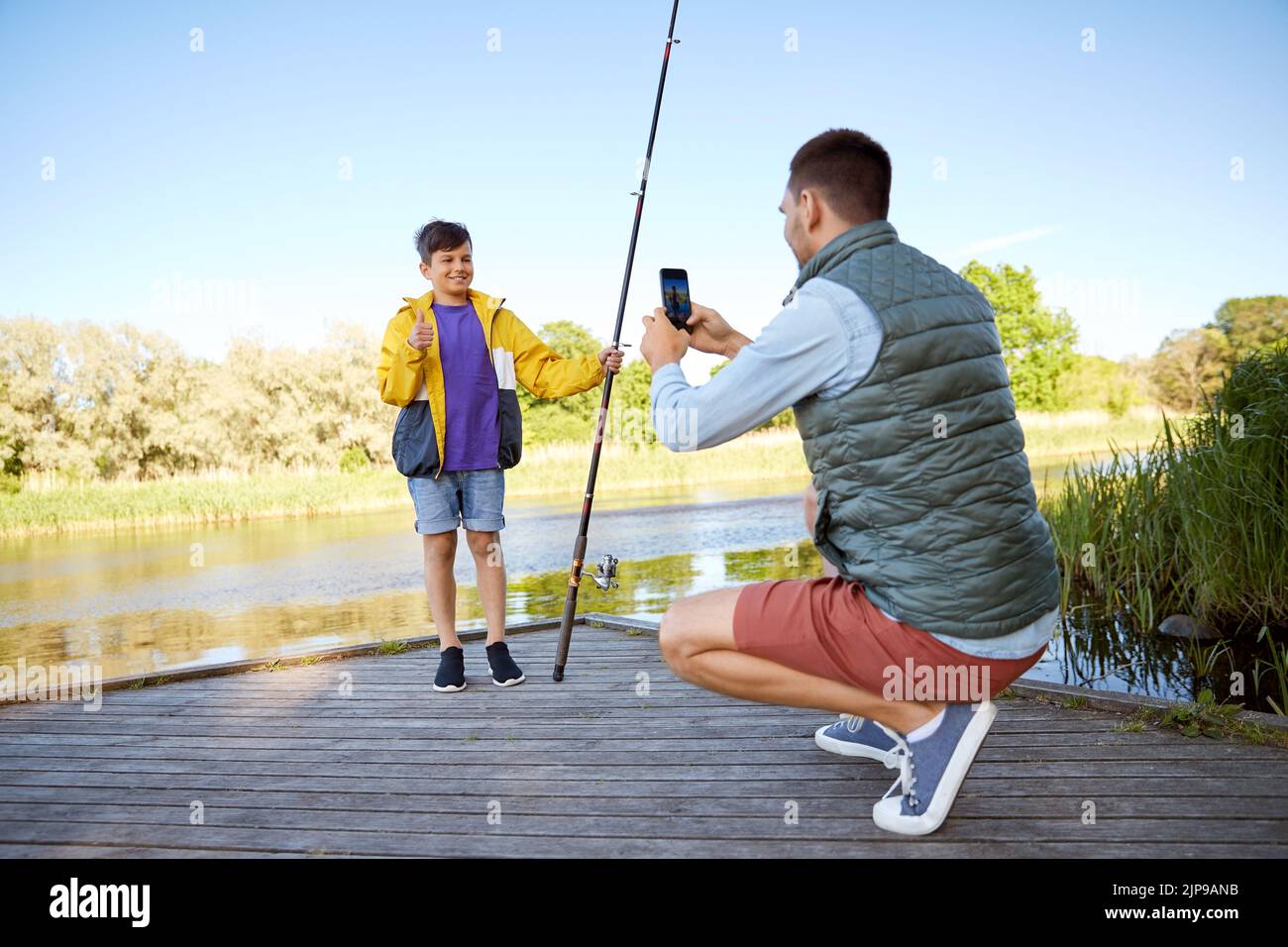 father photographing son with fishing rod on river Stock Photo - Alamy