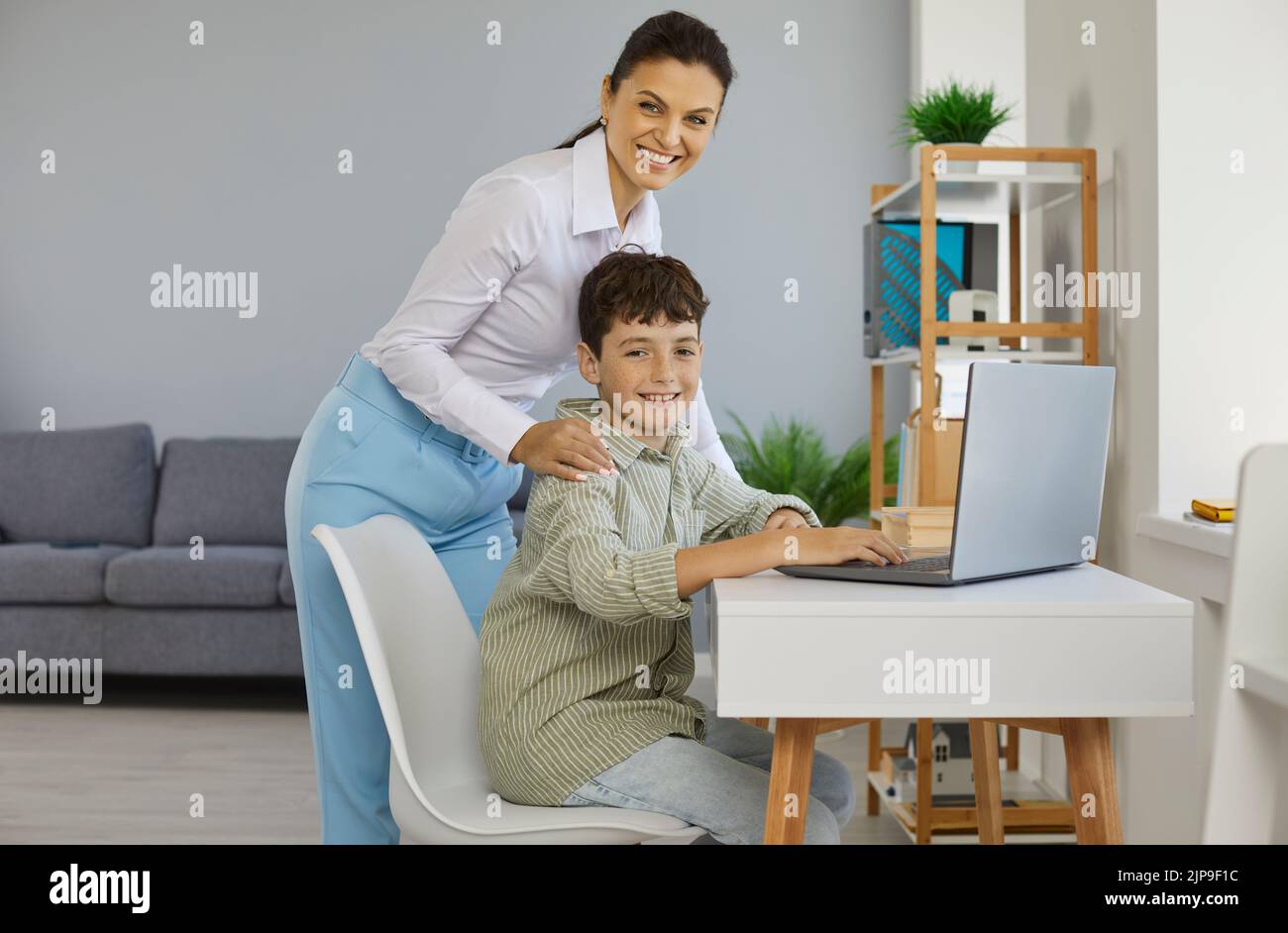 Happy parent or school teacher helping student boy while he uses laptop ...