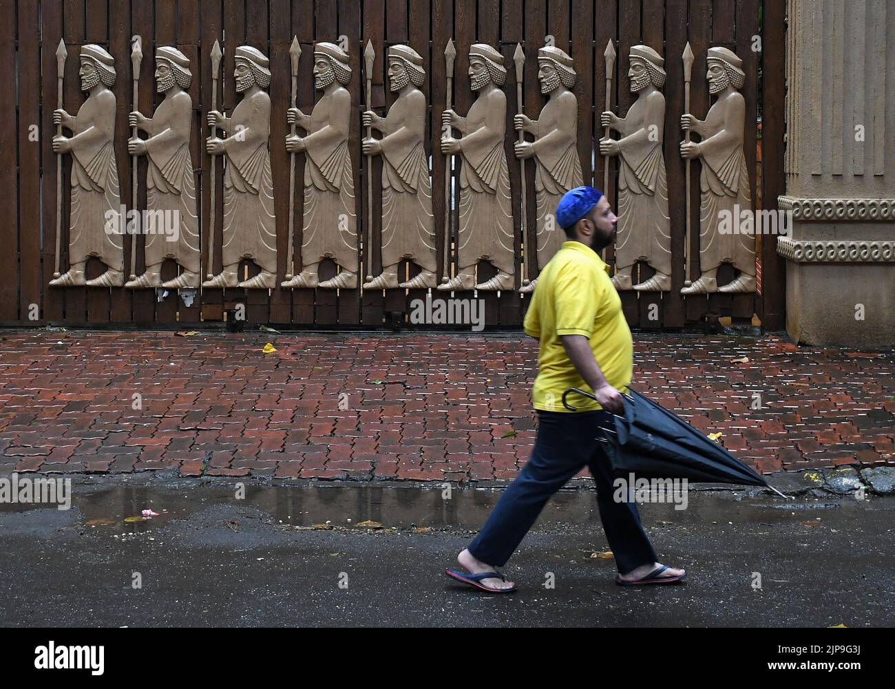 A Parsi man holding an umbrella walks past the carvings of guardians of ...