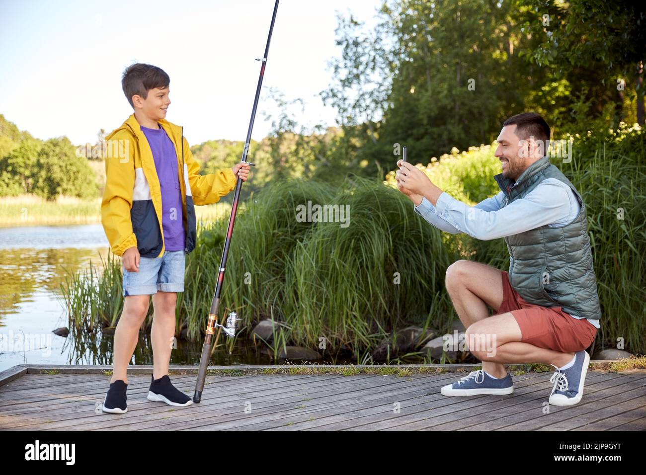 father photographing son with fishing rod on river Stock Photo - Alamy