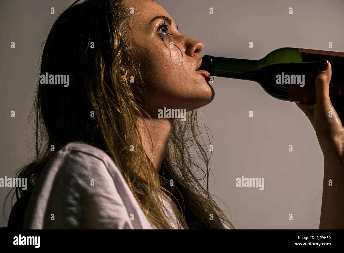 Crying young woman with smeared mascara drinks alcohol from neck of ...