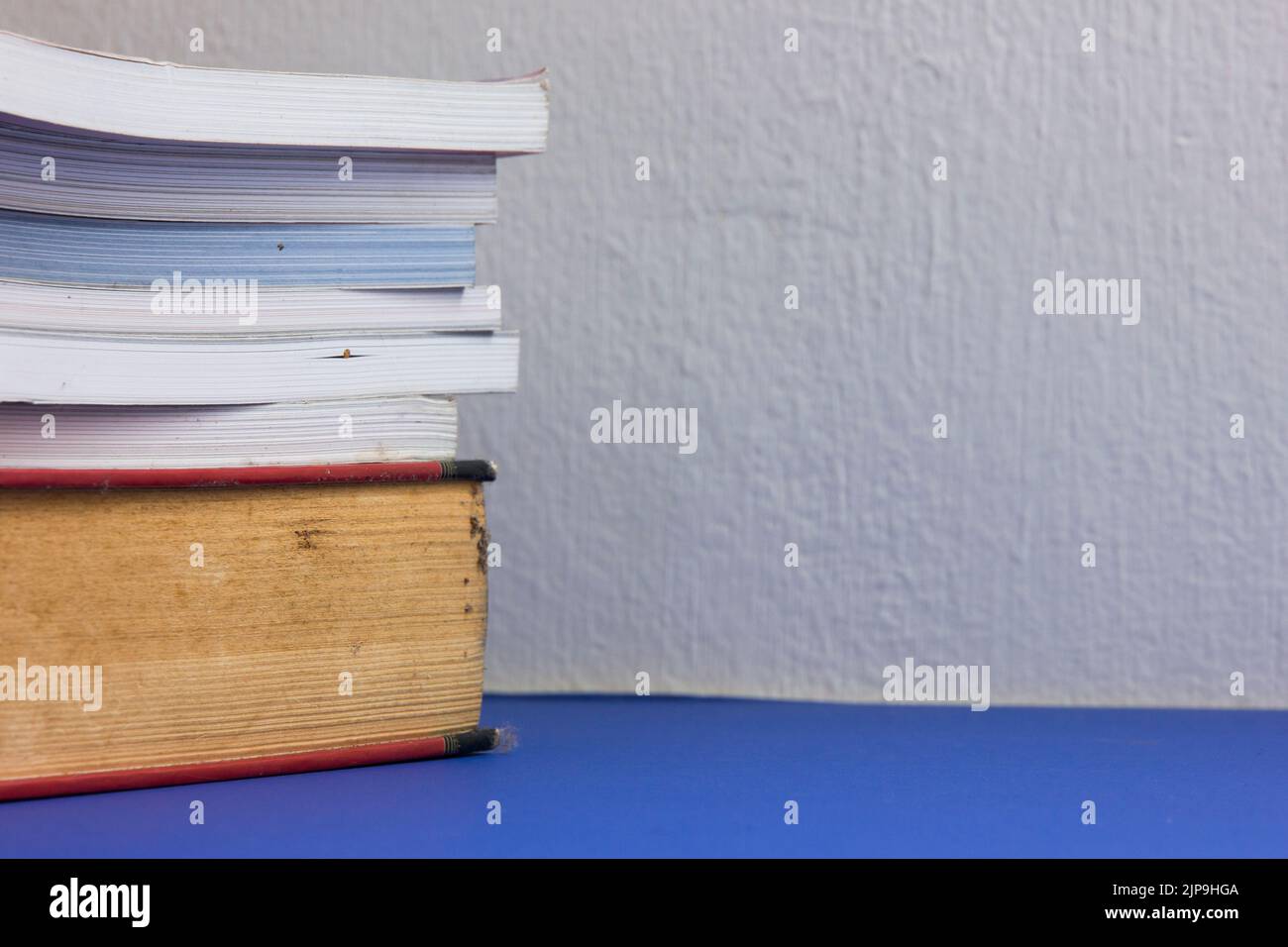 A stack of books on the blue table against a white wall background ...