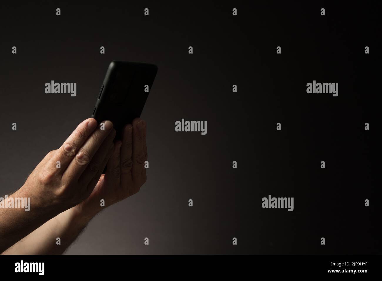 Side view of man's hands holding smart phone isolated on dark ...