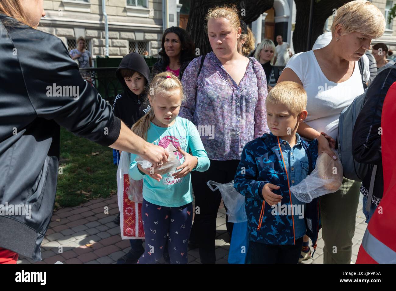 A volunteer distributes loaves of bread to children in a queue during ...