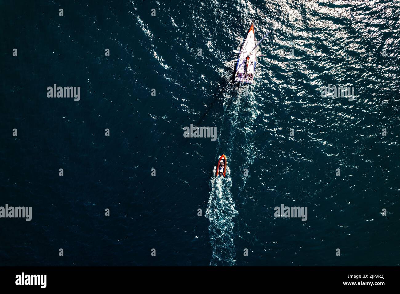 An aerial top view of a yacht dragging a small boat in a deep blue ...