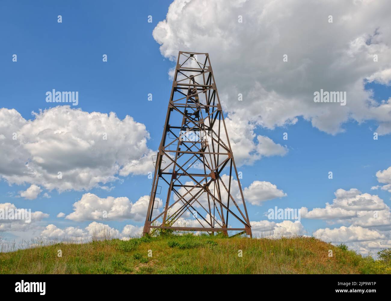 Silhouette of metal geodetic tower is on grassy hillock on blue sky ...