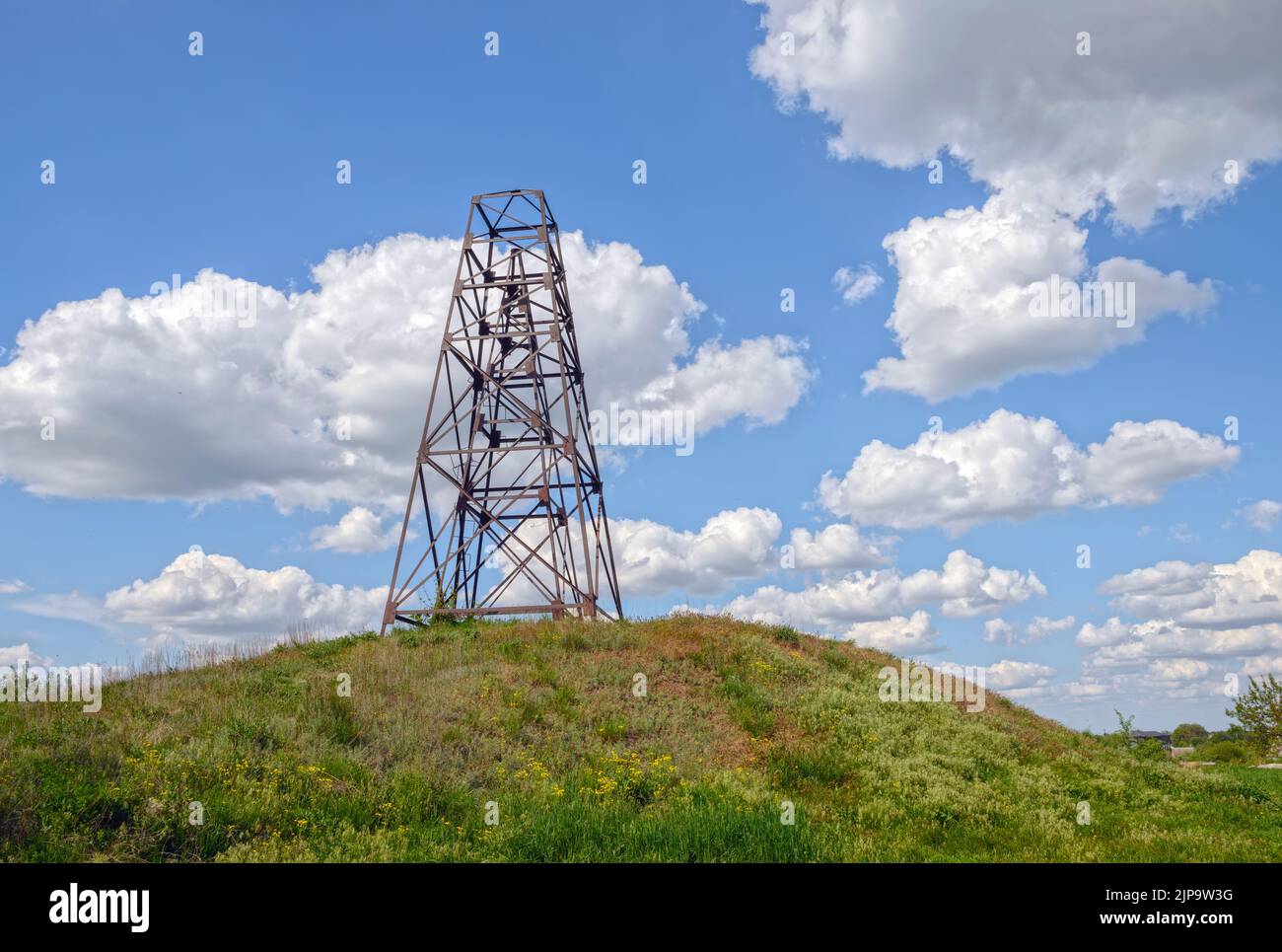 Silhouette of metal geodetic tower is on grassy hillock on blue sky ...