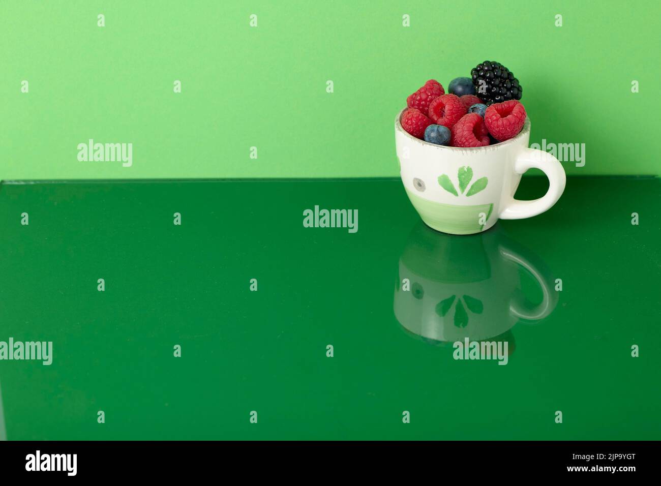 Cup with red fruits on green background with mirror effect Stock Photo ...