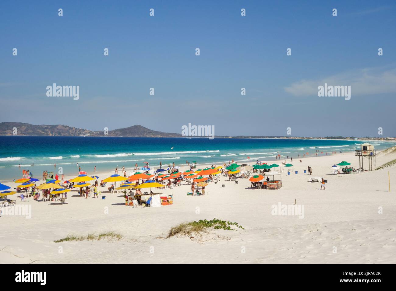 colorful umbrellas and tourists crowd the sand line at Praia do Forte ...
